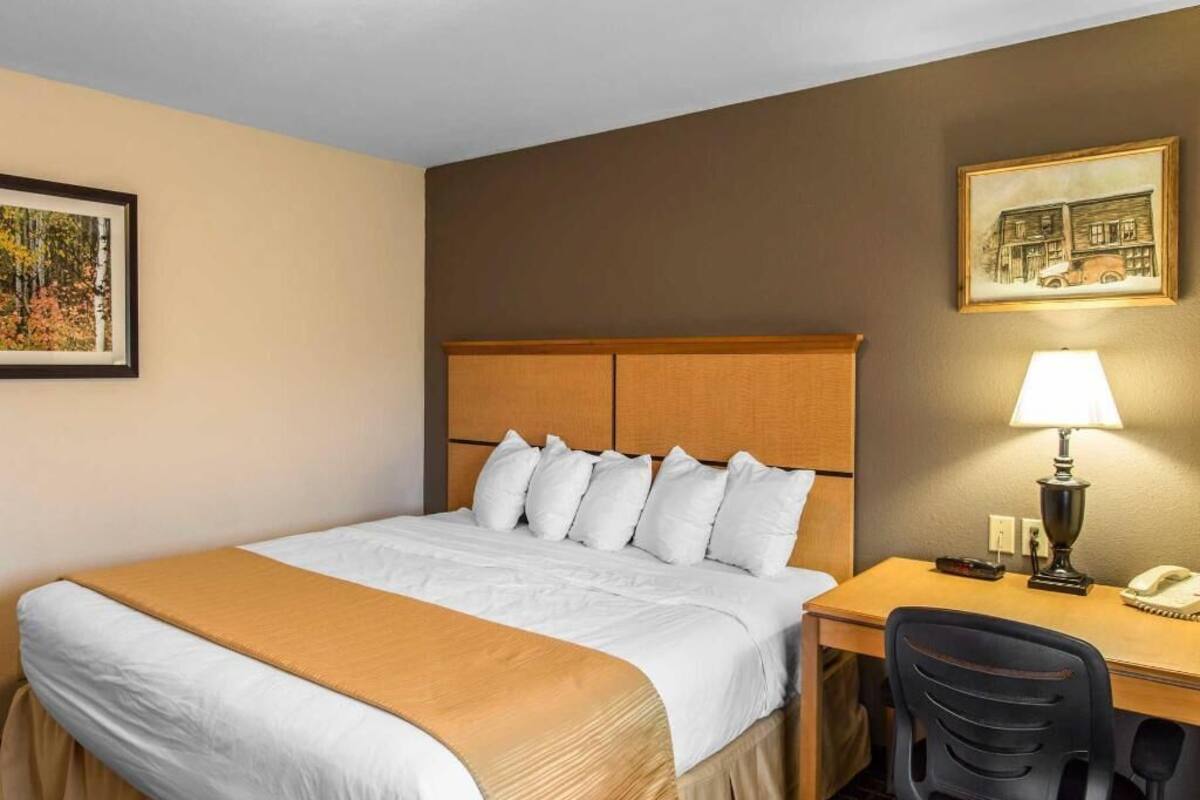 Quarto de hotel com cama, escrivaninha, cadeira, luminária e duas imagens emolduradas nas paredes.
