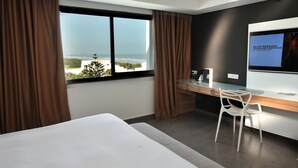 Quarto de hotel moderno com uma cama grande, uma escrivaninha e vista para o oceano.