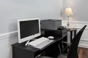 Uma escrivaninha moderna com um computador, impressora, teclado, rato e uma lâmpada.
