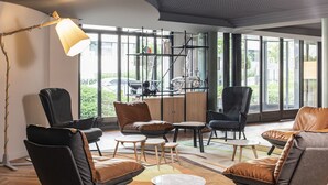 Uma área de estar moderna com poltronas de couro, uma mesa de centro e uma luminária. Há uma janela grande com vista para o exterior.