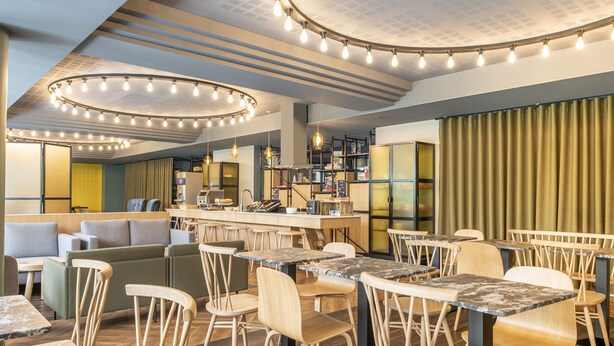 Um restaurante moderno com móveis de madeira, área de bar e um espaço de estar com sofás e mesas.