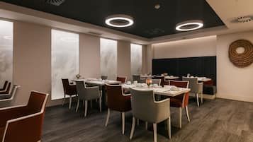 Uma sala de jantar moderna com mesas redondas, cadeiras e teto escuro com luminárias circulares.