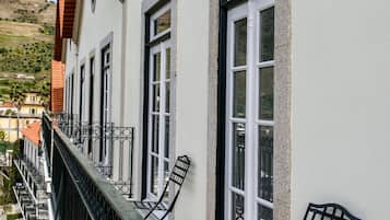 Um edifício com fachada branca, várias janelas e uma varanda com cadeiras.