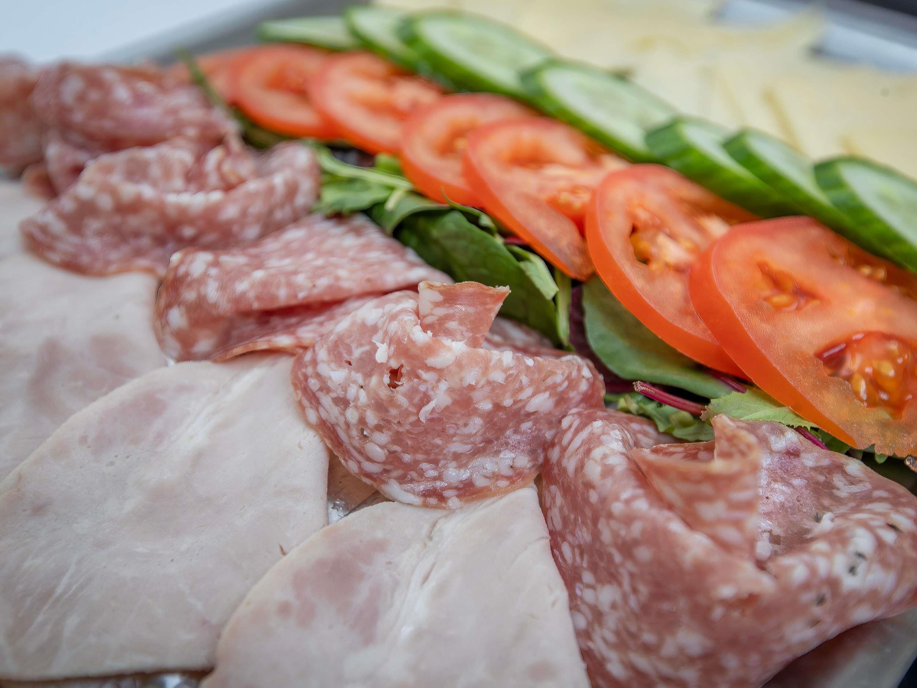 Uma travessa com fatias de salame, tomates frescos e folhas verdes.