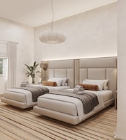 Quarto de hotel moderno com duas camas, uma janela grande com cortinas, luminária pendente e tapete listrado.