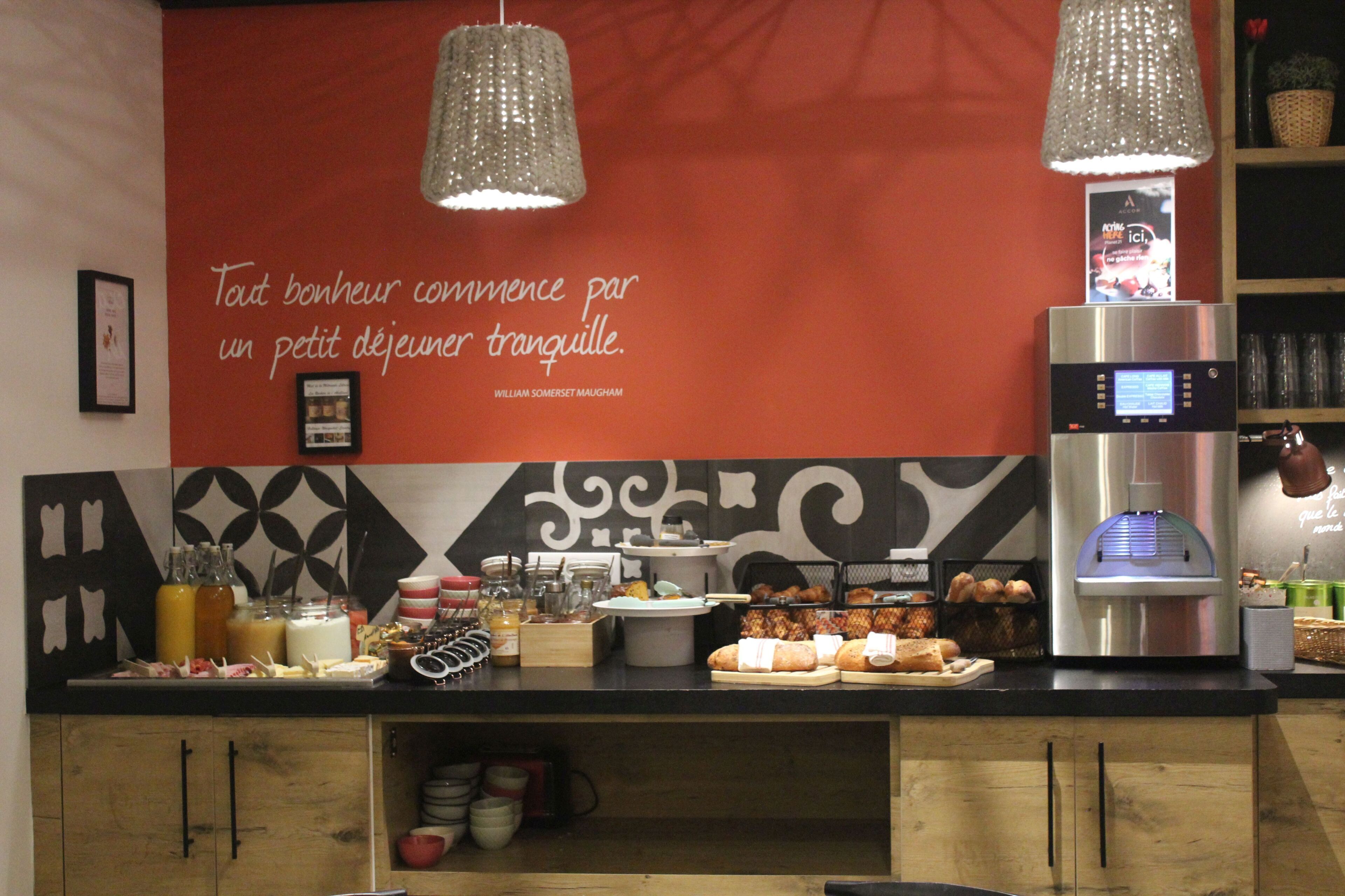 Um buffet de café da manhã com diversas opções de alimentos, uma máquina de café e uma parede decorativa com uma frase.