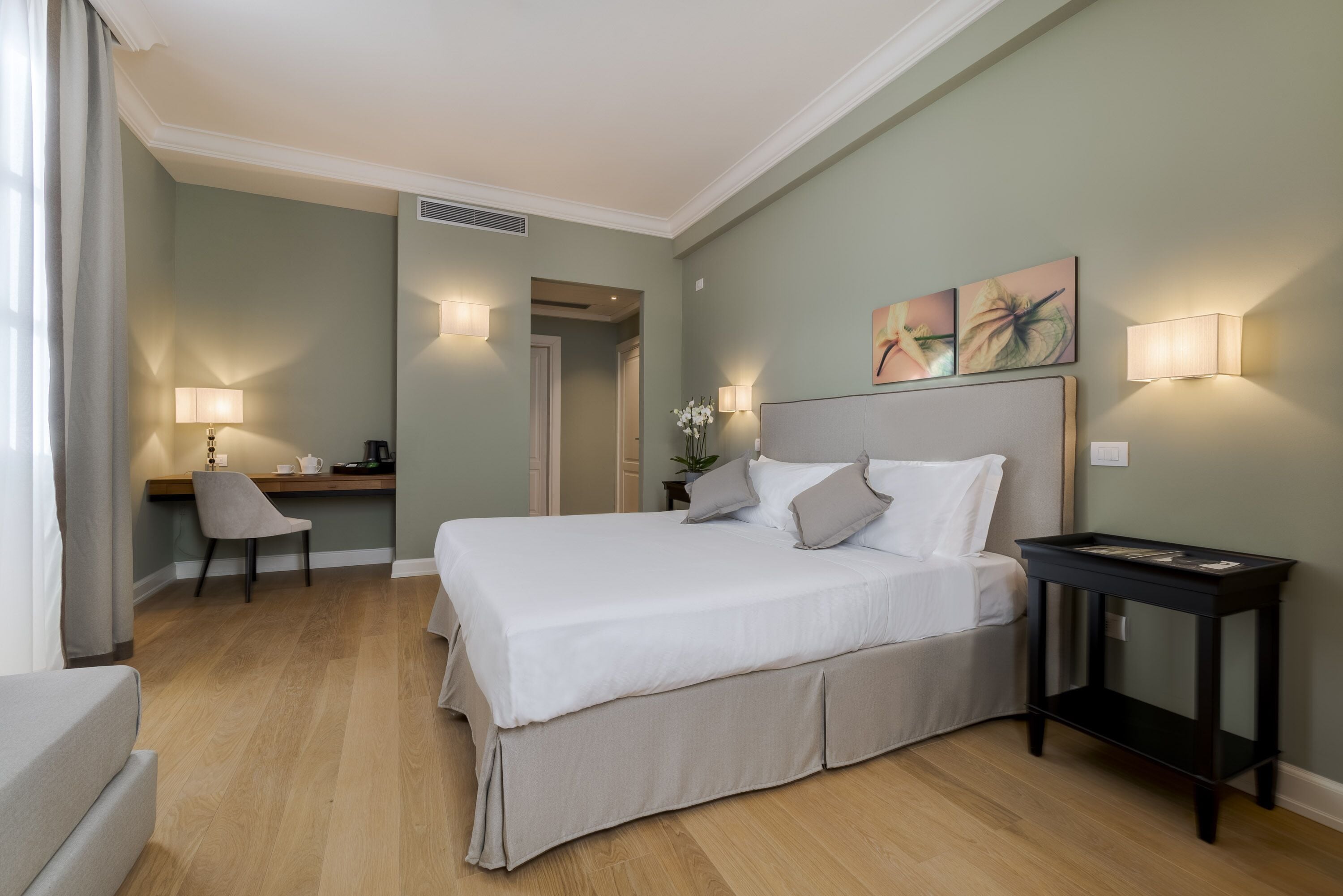 Quarto de hotel com uma cama grande, uma escrivaninha com cadeira e uma mesinha.