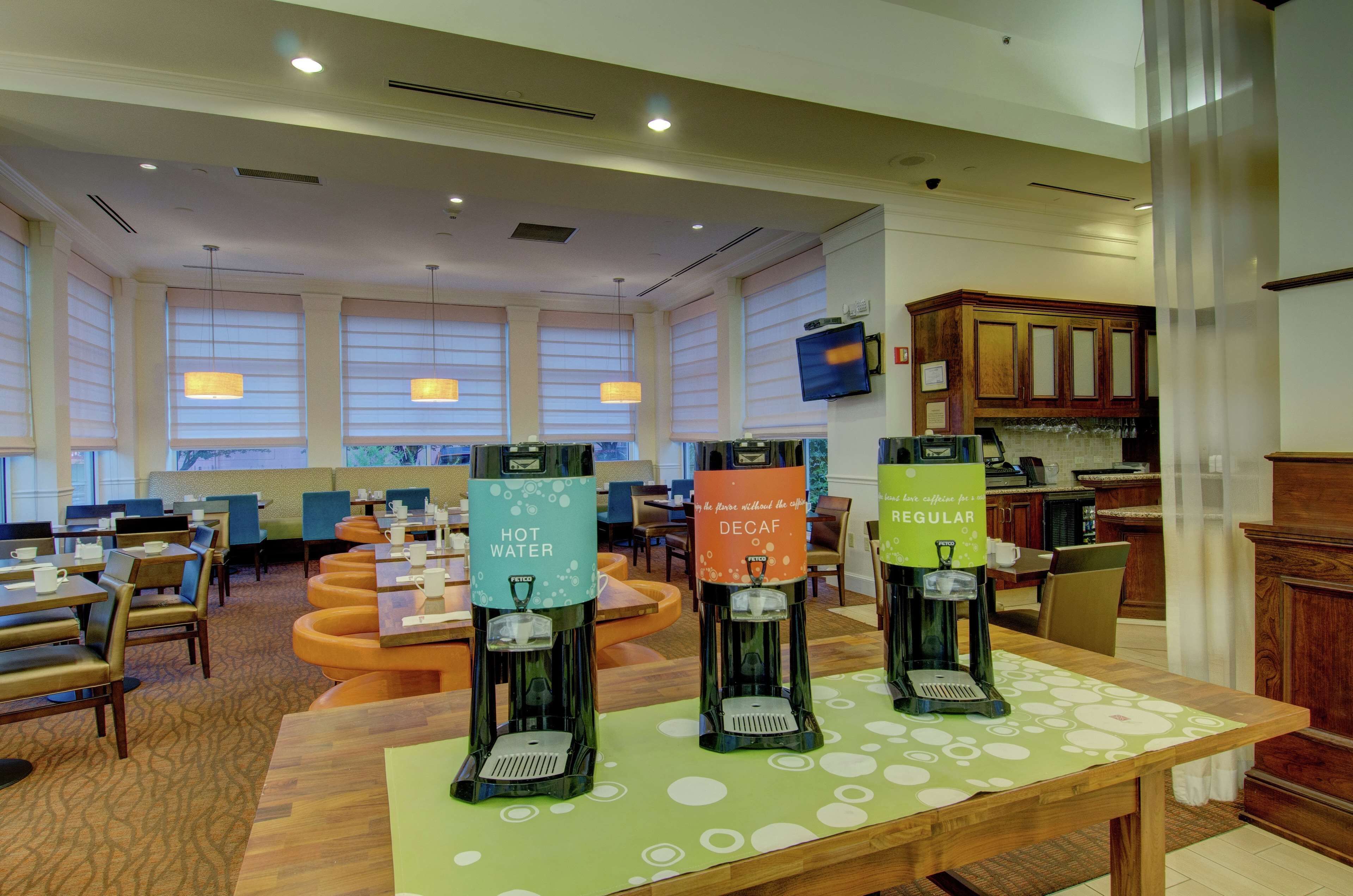 Um saguão de hotel com um bar de café, área de estar e uma cozinha ao fundo.