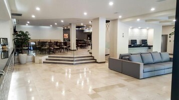 Um hall amplo com design moderno, apresentando uma área de estar com sofás e uma escadaria que leva a uma sala de jantar.