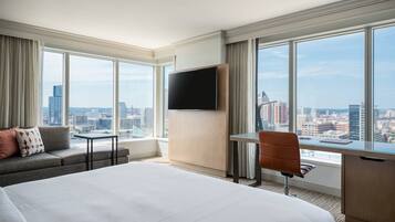 Quarto de hotel com uma cama grande, uma escrivaninha, uma cadeira, uma televisão e vista para a cidade.