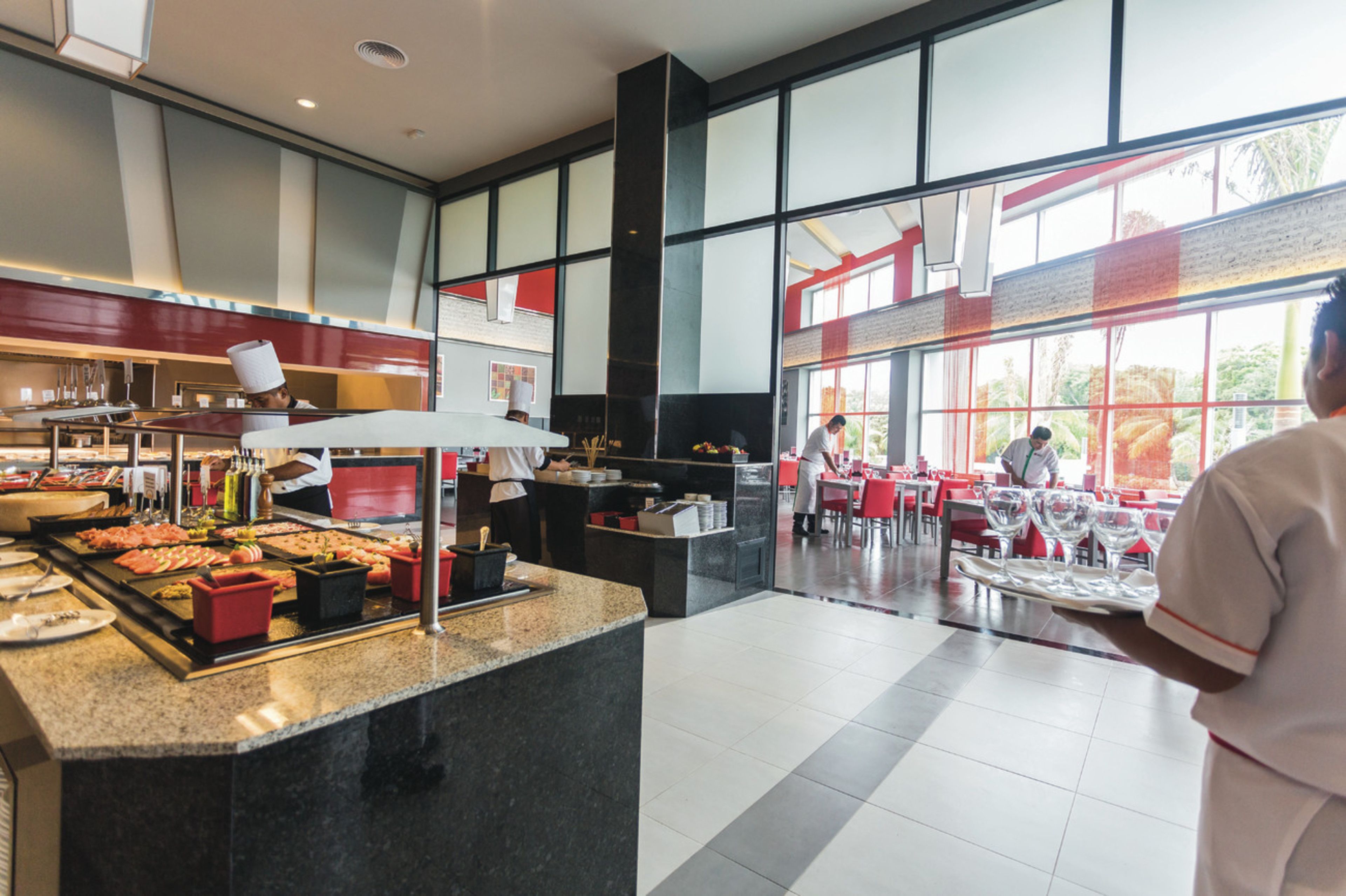 Um restaurante moderno com balcão central, decoração em vermelho e branco e grandes janelas.
