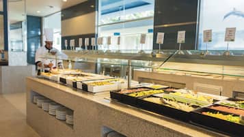 Buffet com diversas opções de comida, um chef uniformizado e vista para o mar através de amplas janelas.