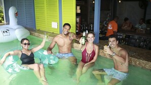 Uma área de piscina com boias de cisne infláveis, um bar e pessoas relaxando.