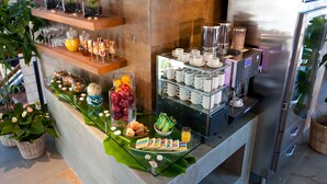 Uma área de buffet com diversos alimentos, copos e uma máquina de café.