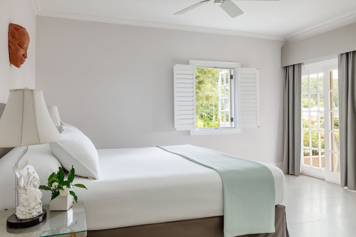 Um quarto com uma cama, mesa de cabeceira, abajur, escultura decorativa e janela com persianas.