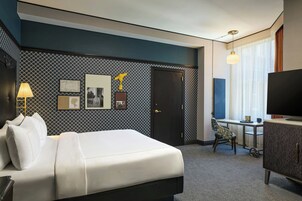 Quarto de hotel com cama, escrivaninha, televisão e guarda-roupa.