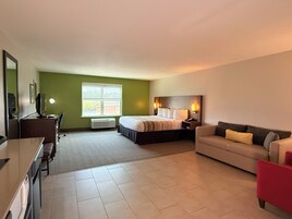 Quarto de hotel com cama, escrivaninha, cadeira, sofá e janela.