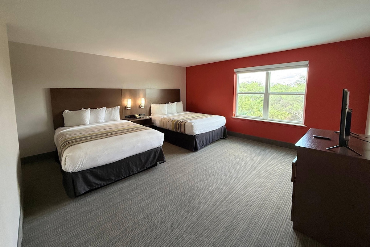 Quarto de hotel com duas camas, uma janela grande e uma escrivaninha com televisão.