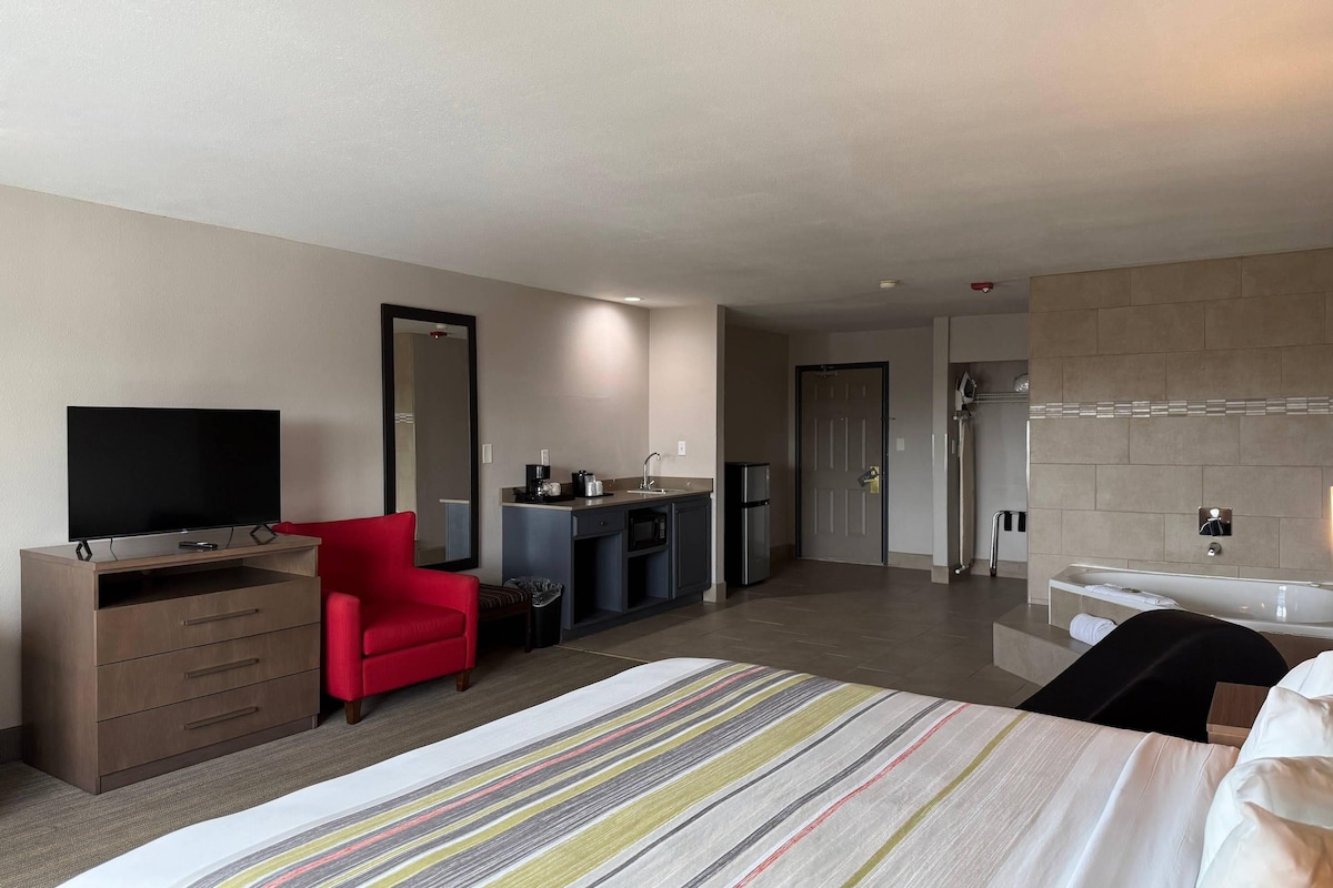Quarto de hotel com cama, televisão, escrivaninha com cadeira, cozinha compacta e banheiro com banheira e pia.