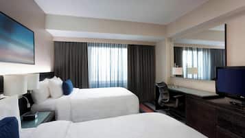 Quarto de hotel com duas camas, uma escrivaninha, uma televisão e um espelho grande.