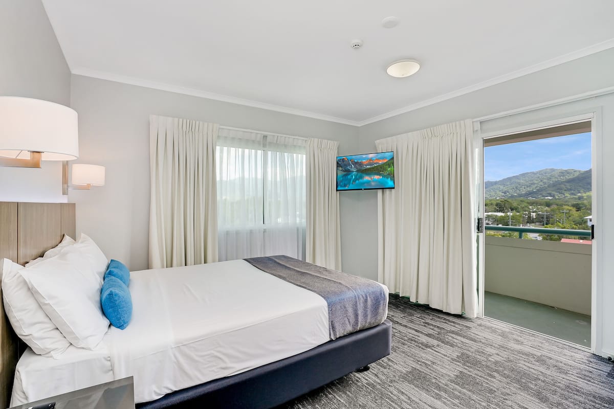 Quarto de hotel com cama, televisão na parede e varanda com vista para as montanhas.