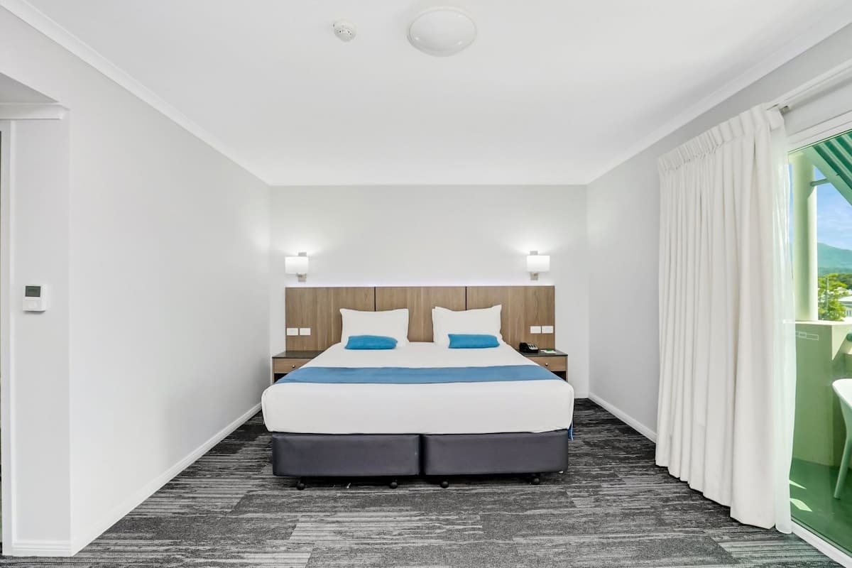 Quarto de hotel com uma cama grande, duas mesas de cabeceira, um termostato e vista para o exterior.