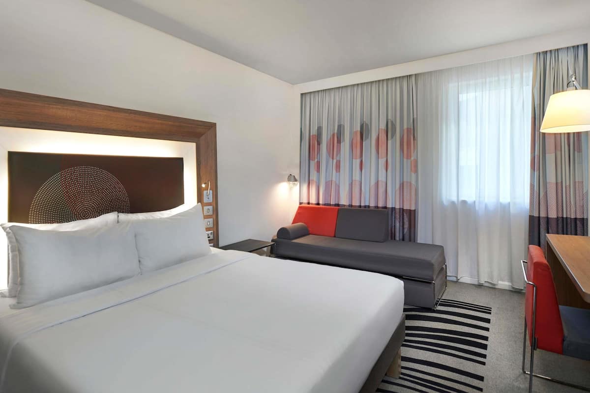 Quarto de hotel com uma cama grande, uma escrivaninha, uma cadeira e um sofá.
