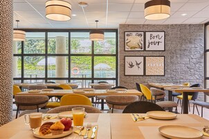 Uma sala de jantar moderna com mesas, cadeiras, janelas amplas e obras de arte nas paredes.