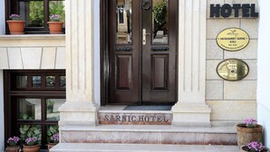 Exterior do Hotel Sarnic, com entrada em madeira escura, uma placa de identificação e degraus que levam à entrada.
