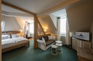 Quarto de hotel com cama, sofá, televisão e uma mesinha.