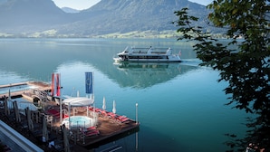Um barco atracado em uma marina, com montanhas ao fundo, área de piscina com guarda-sóis e espreguiçadeiras.