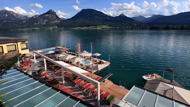 Um hotel na beira do lago com piscina, espreguiçadeiras e um cais para barcos.