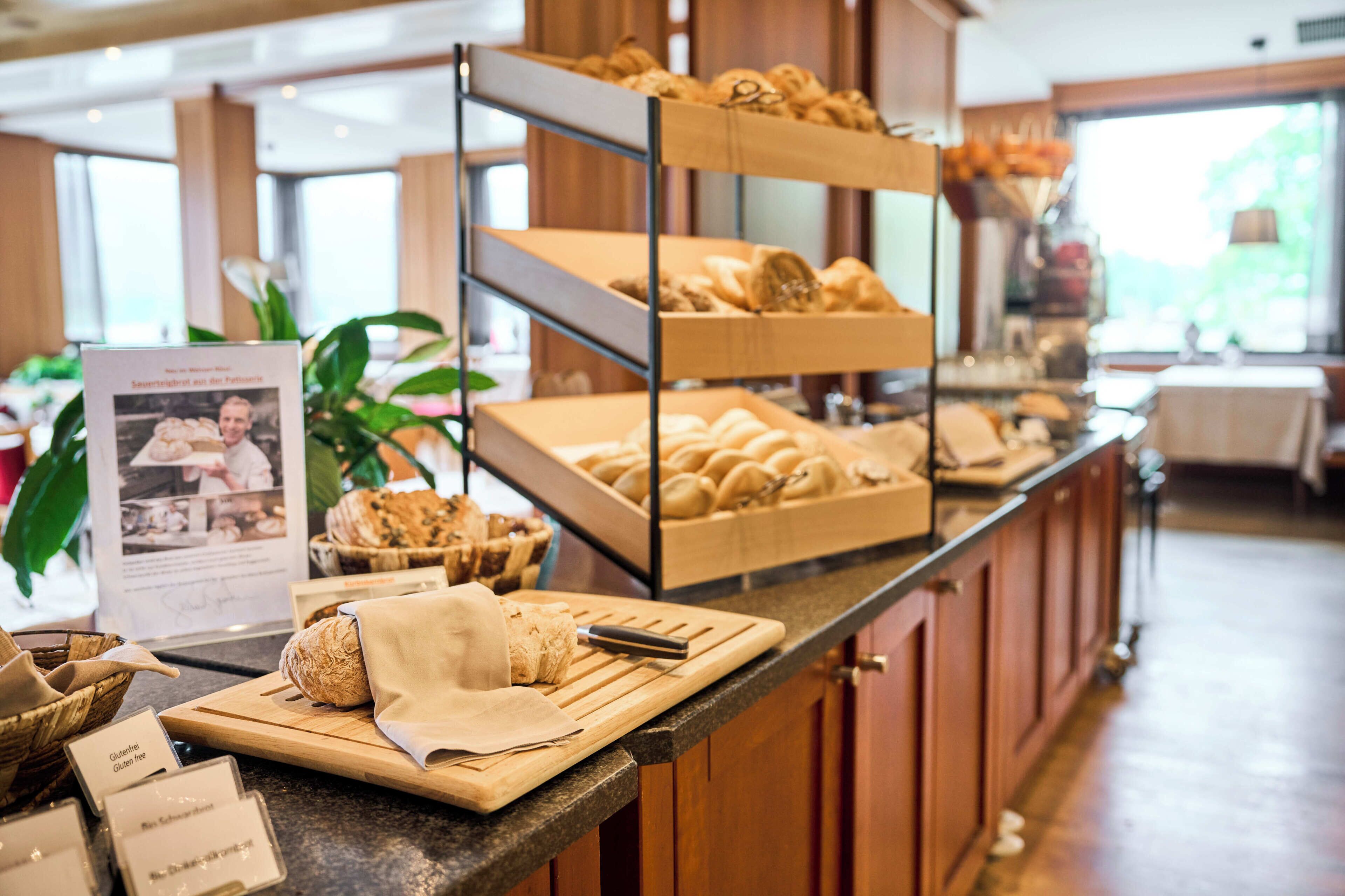 Balcão de buffet com diversos produtos de panificação e placa indicando opções sem glúten.