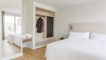 Quarto de hotel com uma cama grande, um guarda-roupa com espelho e uma pequena mesa com abajur.