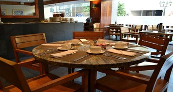 Mesa redonda de jantar com cadeiras, xícaras, pires e talheres organizados.