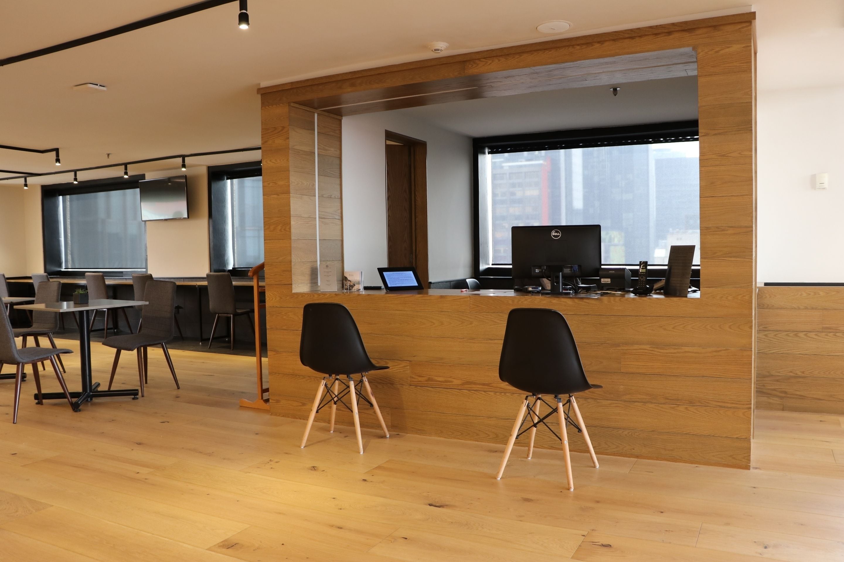 Um espaço de escritório moderno com uma mesa de recepção, duas cadeiras pretas, um laptop e um computador desktop.