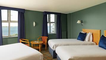 Quarto de hotel com duas camas, uma mesinha, uma cadeira e vista para o mar.