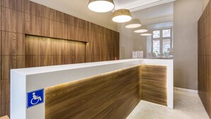 Bancada de recepção com painel de madeira, sinal de acessibilidade para cadeiras de rodas e iluminação pendente.