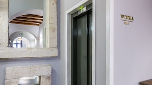 Um elevador moderno com porta de vidro, espelho emoldurado em pedra e uma placa na parede com a inscrição 