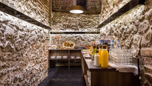 Quarto com paredes de pedra, um balcão para refeições, prateleiras com pratos e diversas opções de comida e bebida.