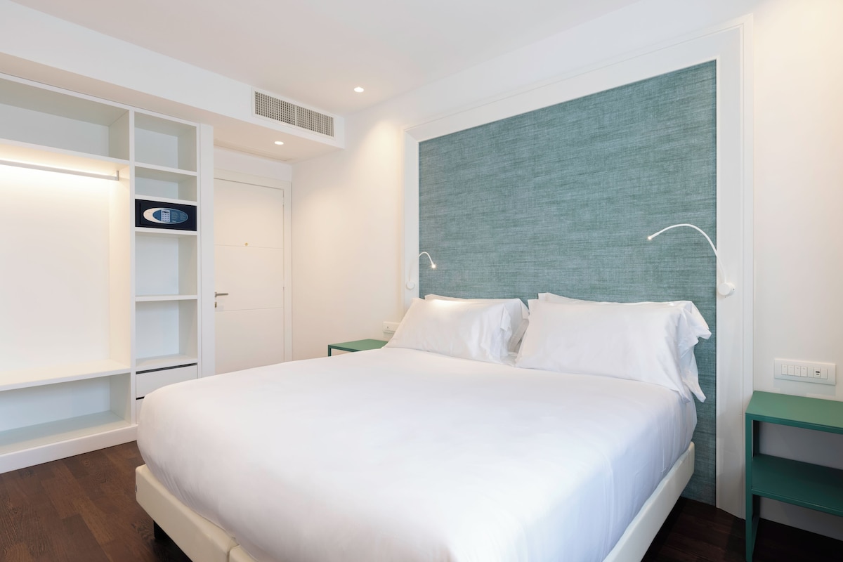 Quarto moderno com cama grande, roupeiro embutido e cabeceira cinza.