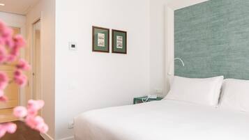Quarto de hotel com uma cama, cabeceira verde, mesa de cabeceira com telefone e duas fotografias emolduradas na parede.