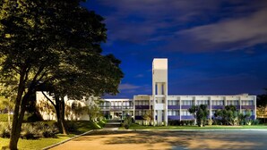 Um hotel moderno com uma torre central, vários andares e um jardim bem cuidado.