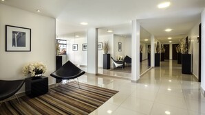 Um lobby moderno com uma mesa de recepção, cadeiras pretas, um tapete listrado e quadros nas paredes.
