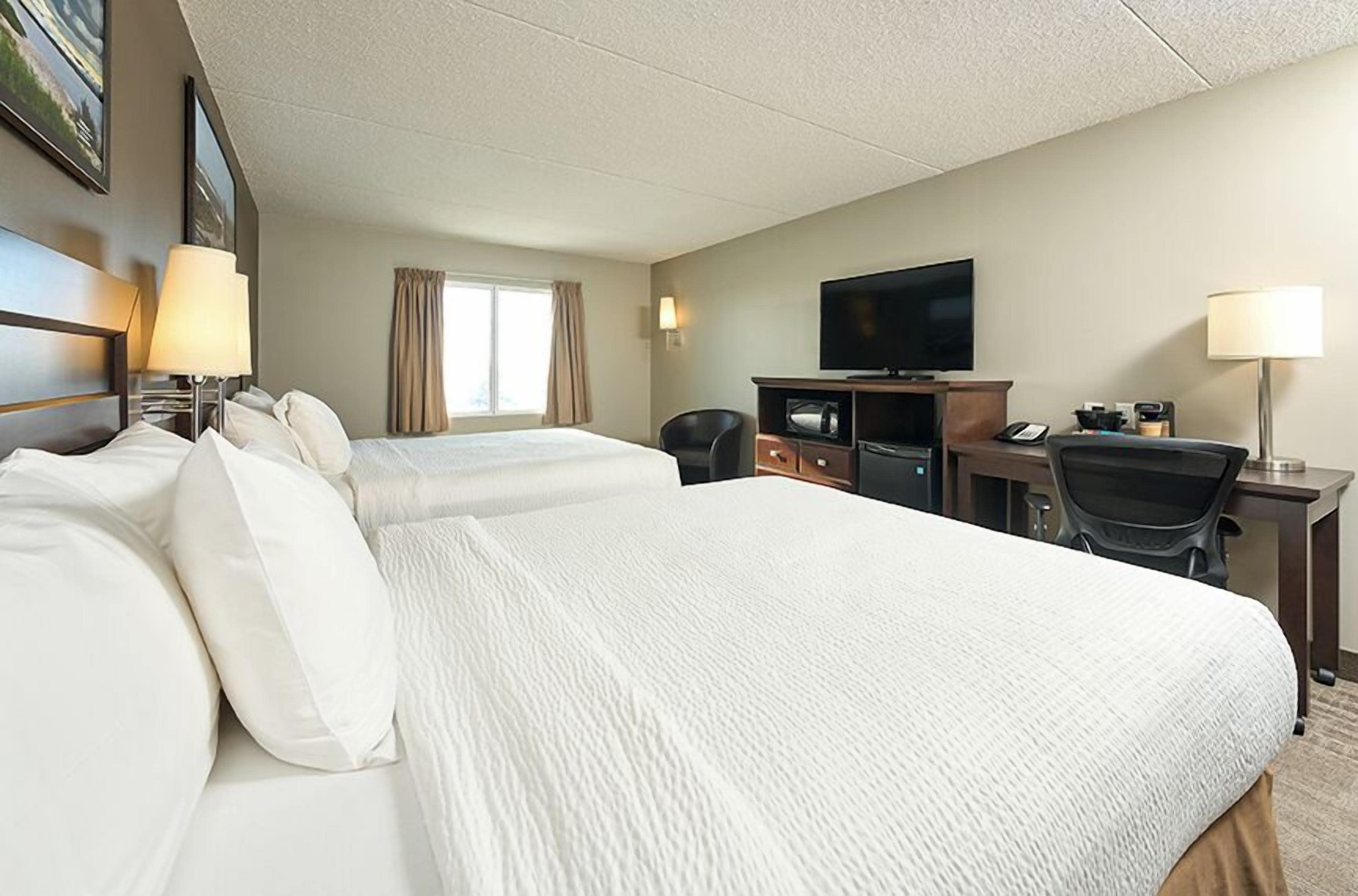Quarto de hotel com duas camas, uma escrivaninha com computador, televisão e uma cadeira.
