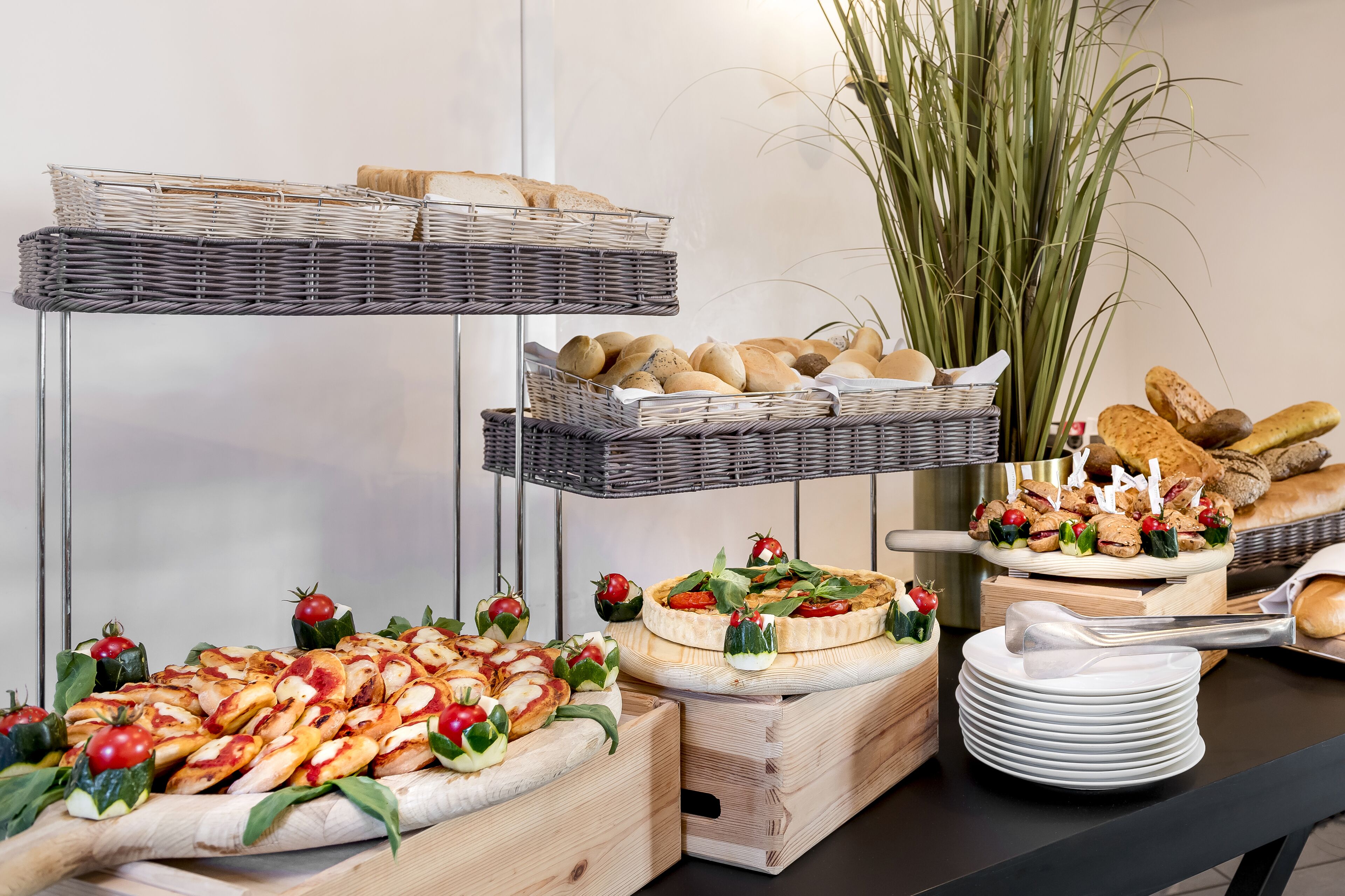 Uma mesa de buffet com diversos alimentos, incluindo pão, doces e uma torta coberta de fruta, dispostos sobre caixas de madeira e cestos de vime.