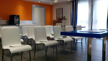 Uma sala de conferências com cadeiras brancas, uma mesa azul e uma máquina de café.