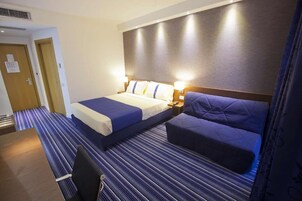 Quarto de hotel com cama, área de estar, escrivaninha e porta.