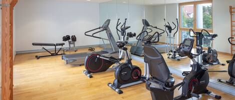 Uma academia com diversos equipamentos de exercício, piso de madeira e um amplo espelho.
