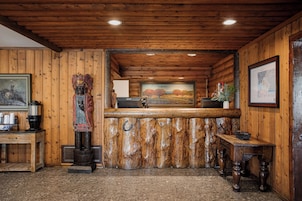 Interior rústico com paredes e teto de madeira, área de bar e uma pintura na parede.